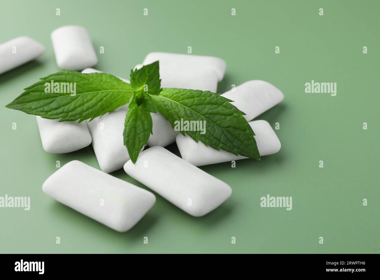 Tasty white chewing gums and mint leaves on light green background ...