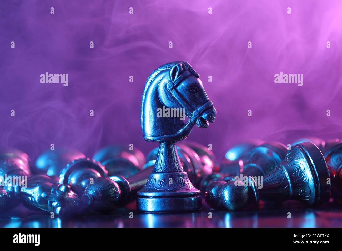 Metal knight among fallen chess pieces on checkerboard in color light ...