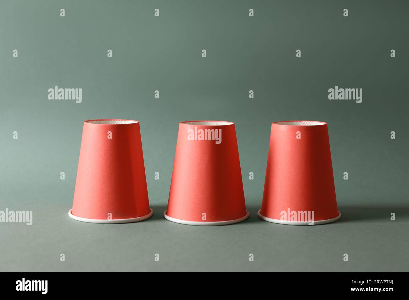 Three red cups on pale olive background. Thimblerig game Stock Photo ...