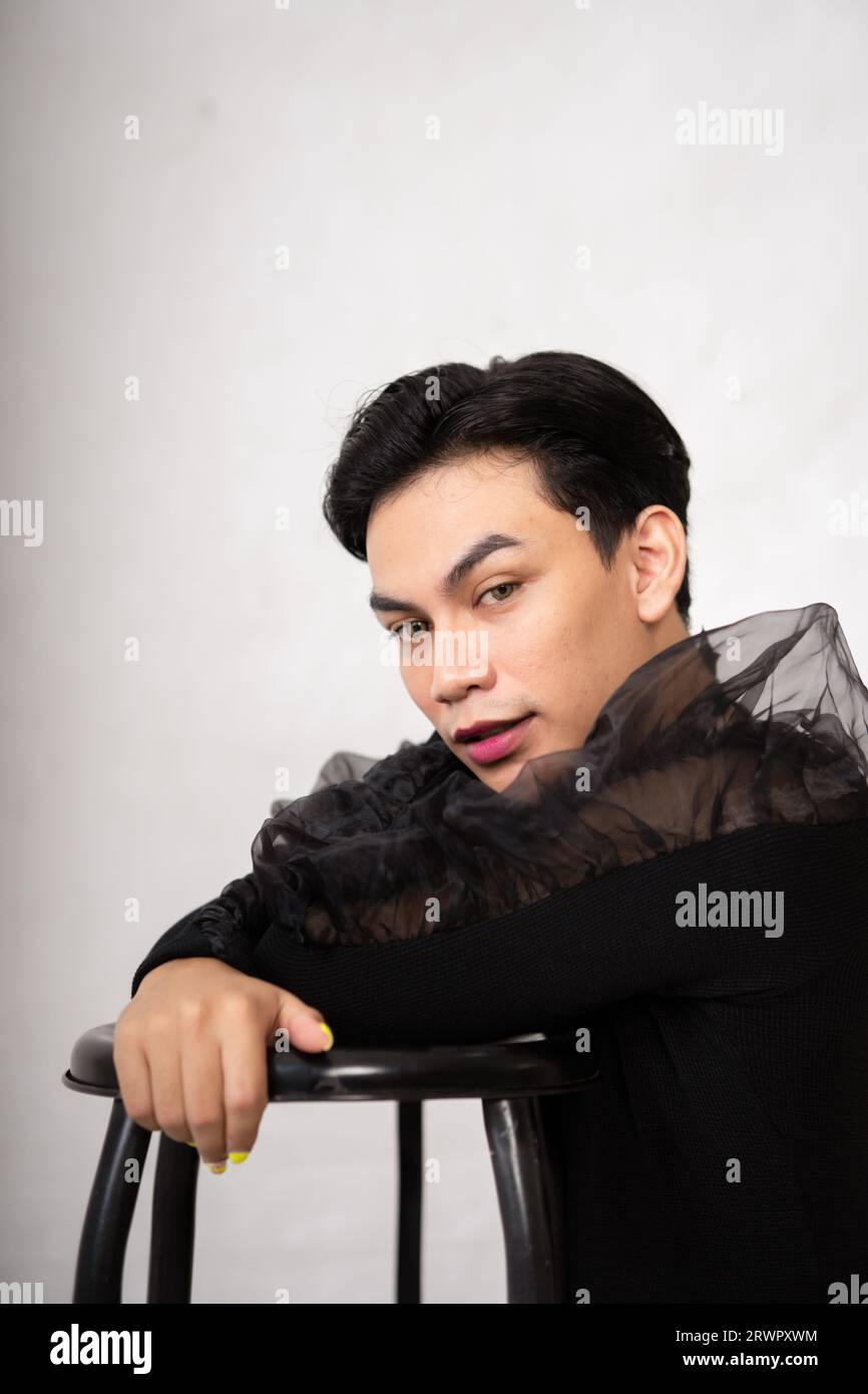 Pretty Asian man putting his hand and head on the chair while posing in ...