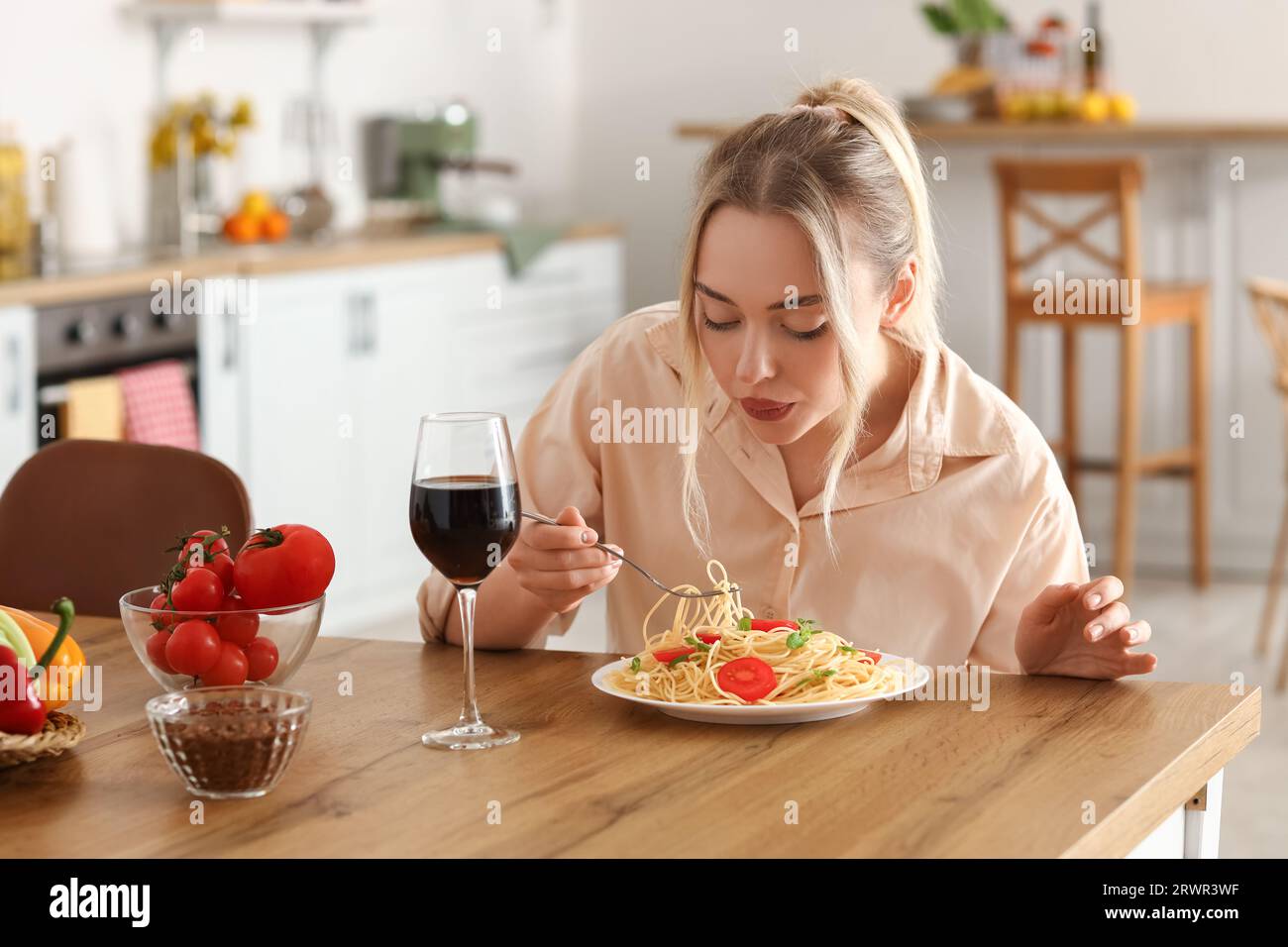 Young woman eating tasty pasta in kitchen Stock Photo - Alamy
