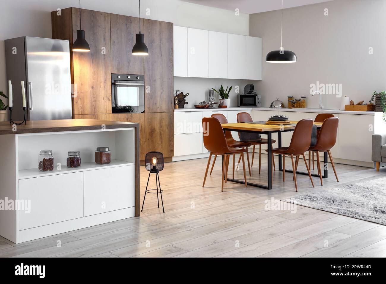 Interior of modern kitchen with dining table, island and glowing lamps ...