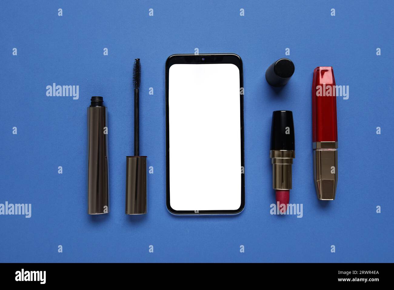 Composition with modern mobile phone, lipsticks and mascara on color ...