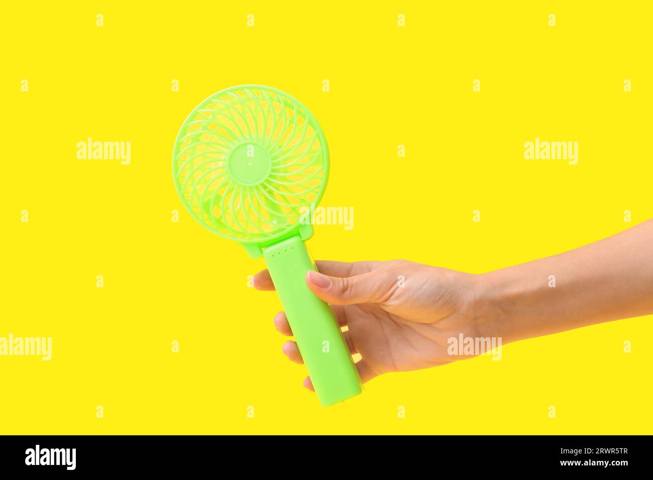 Female hand holding portable green electric fan on yellow background ...