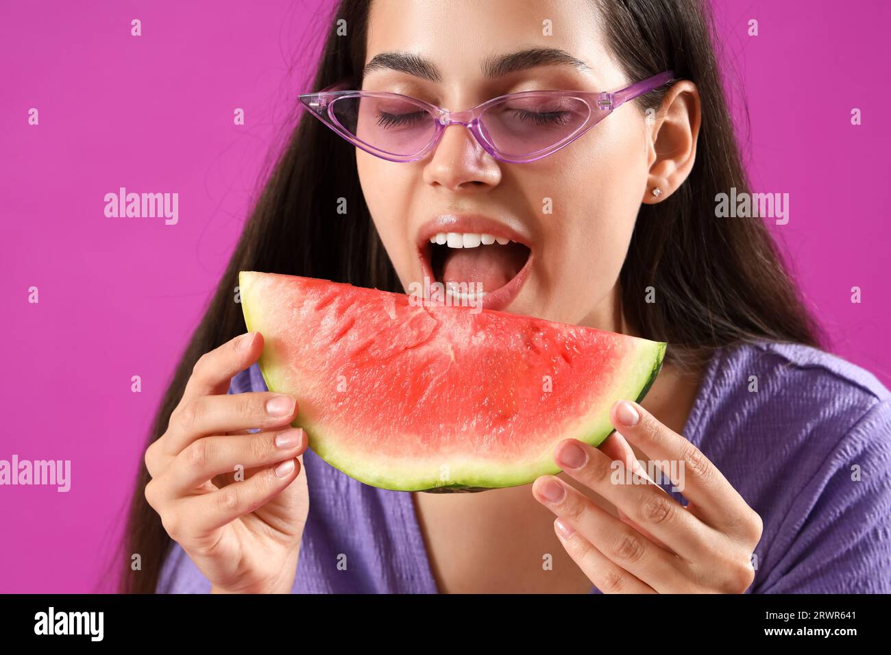Beautiful young woman eating slice of fresh watermelon on purple ...