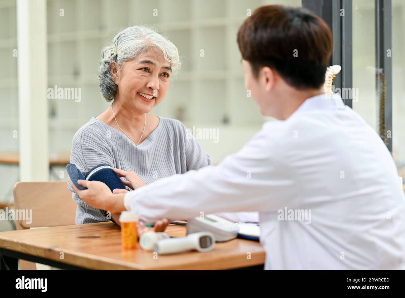 A happy Asian retired old lady is being measured for her heart rate and ...