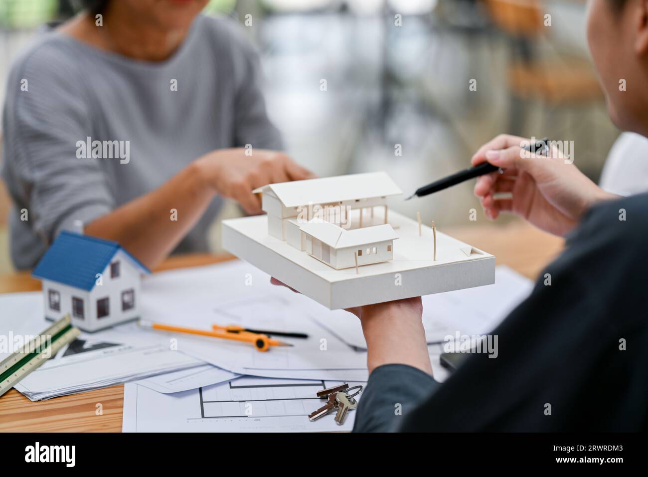 A professional Asian male architect is showing a house model to a ...