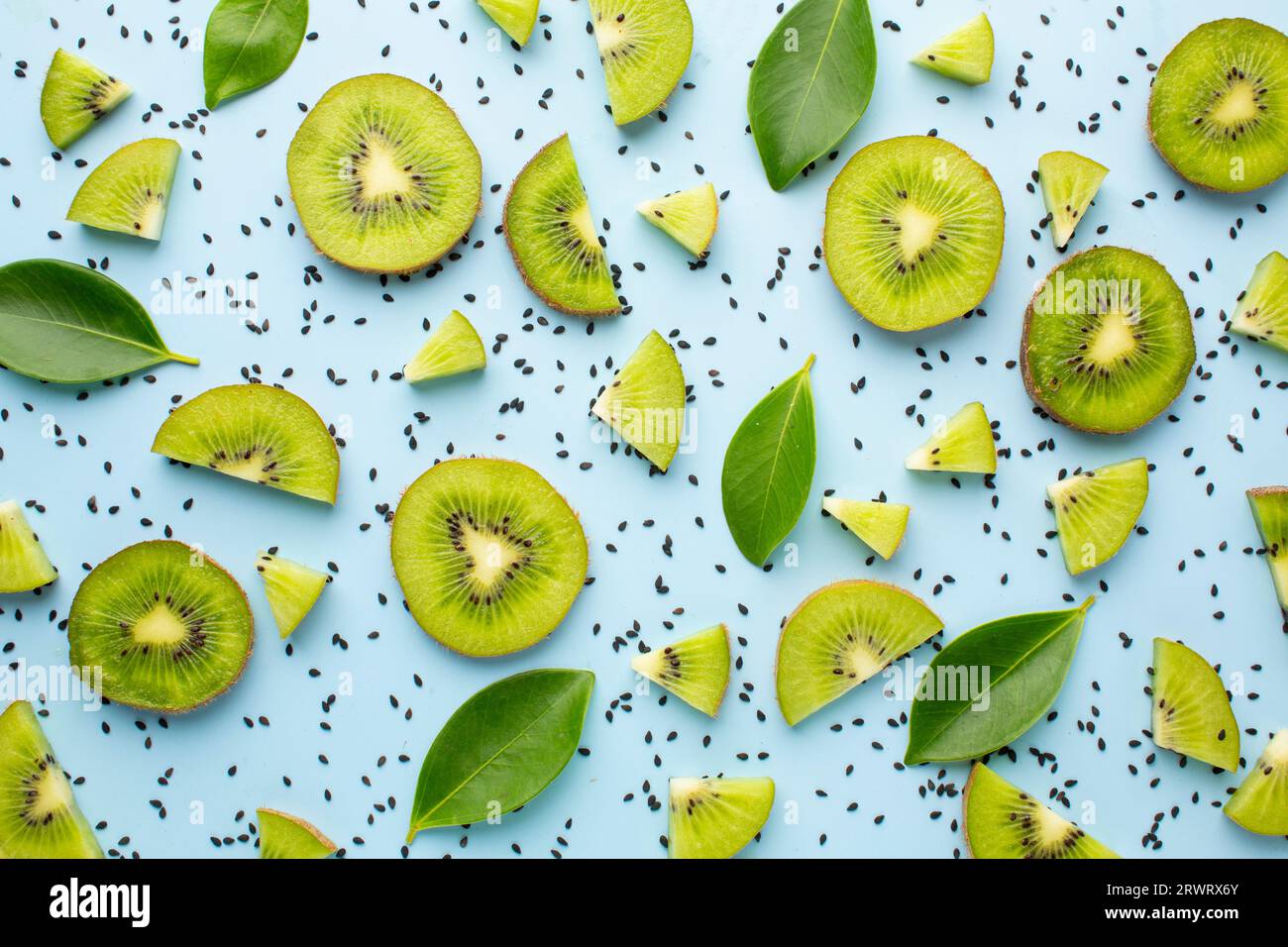 Lay flat of a cut kiwi fruit with seeds on a aqua color solid ...