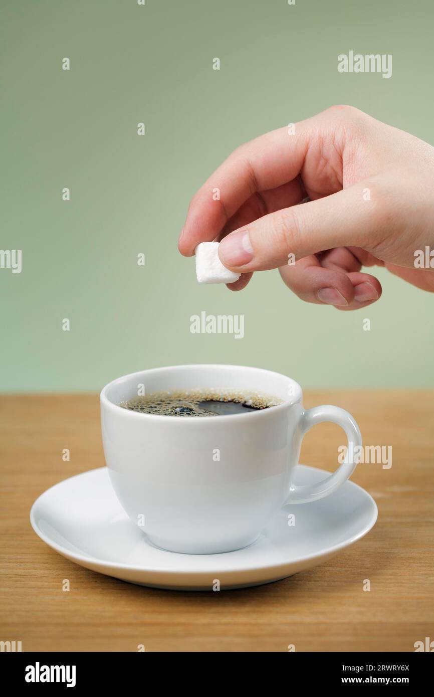A Hand adding sugar to a cup of black coffee Stock Photo - Alamy