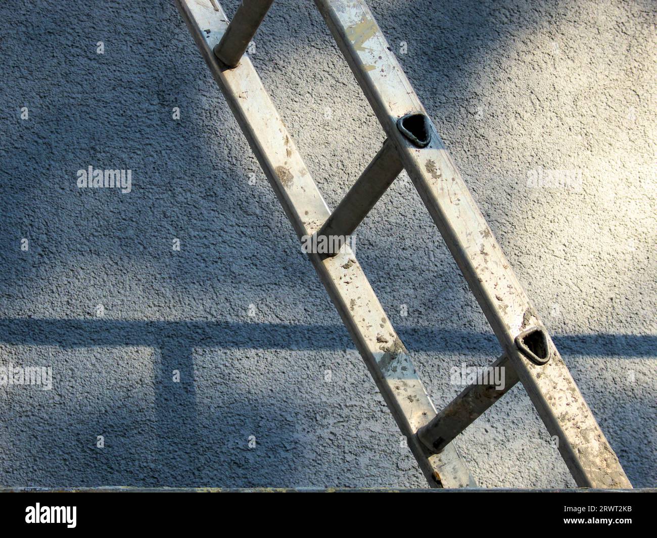 Metal scaffolding ladder leaning against a house wall, with shadow cast ...