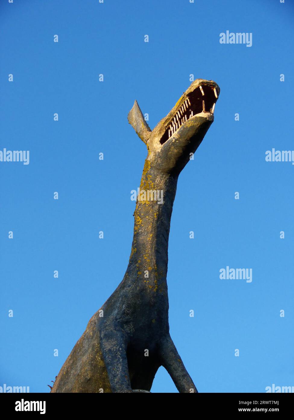 Stone dinosaur rearing up, baring its teeth, blue sky in the background ...