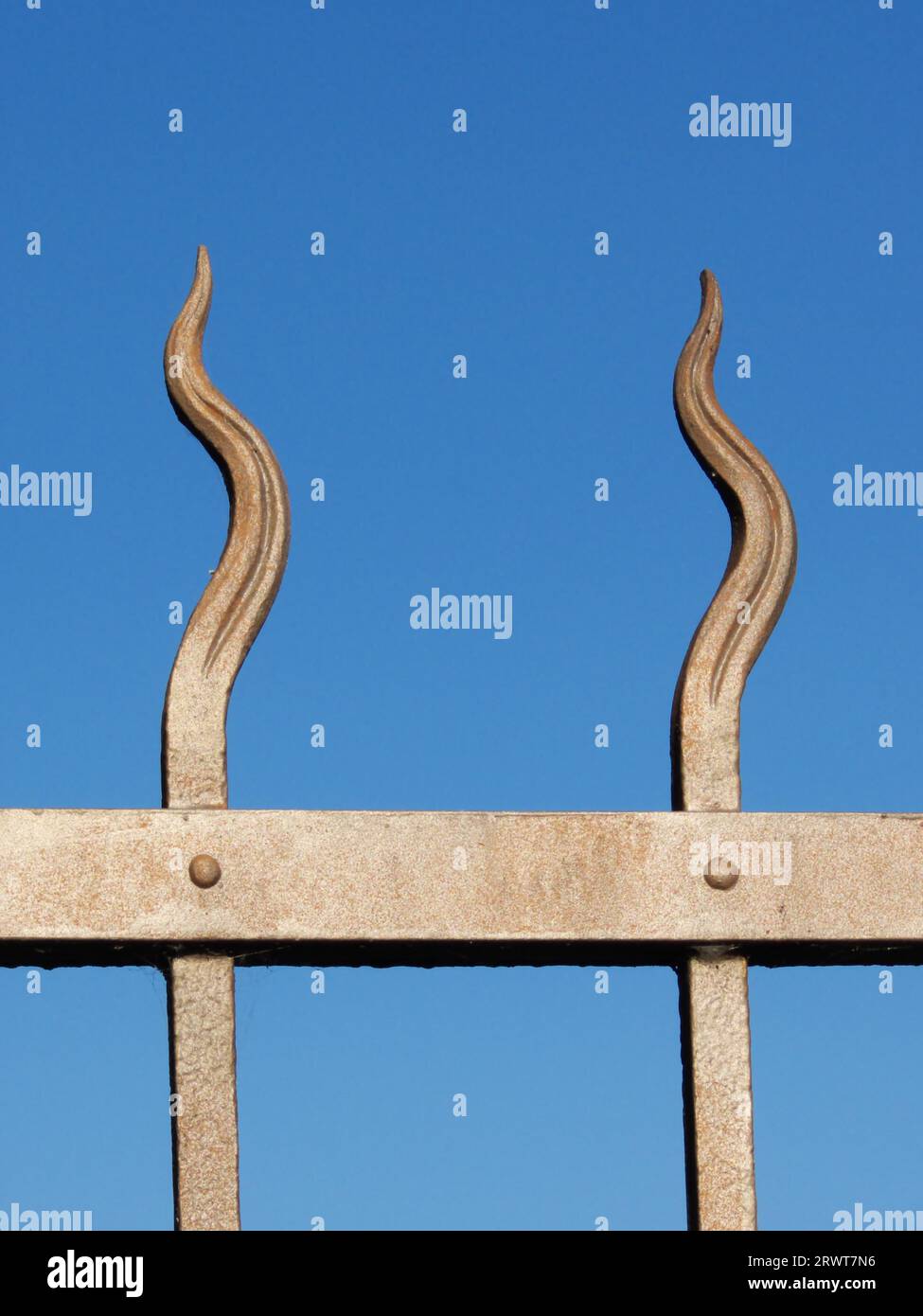 Two struts of a metal curved ornamental fence, background blue sky ...