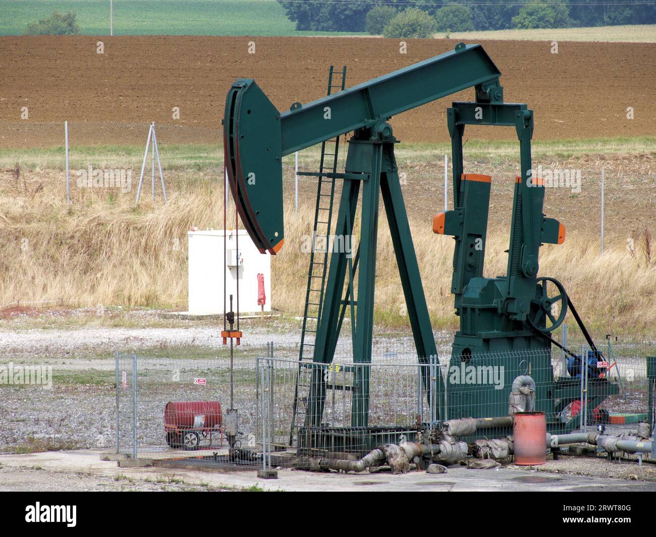 Green oil pump at work, fields, forest and meadow in the background ...