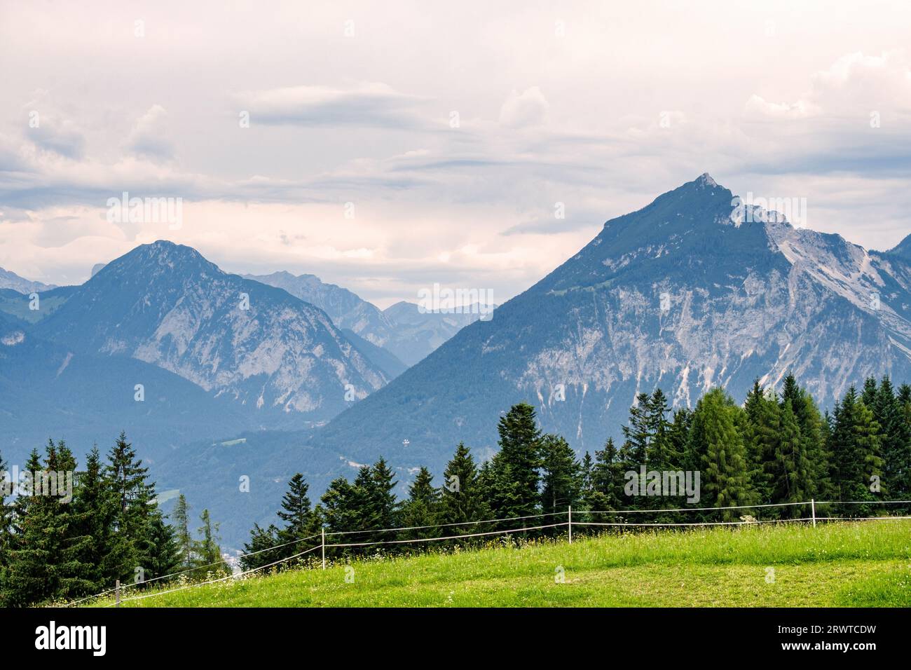 Fields with a fence, treeline & tall mountain peaks in Reith im ...