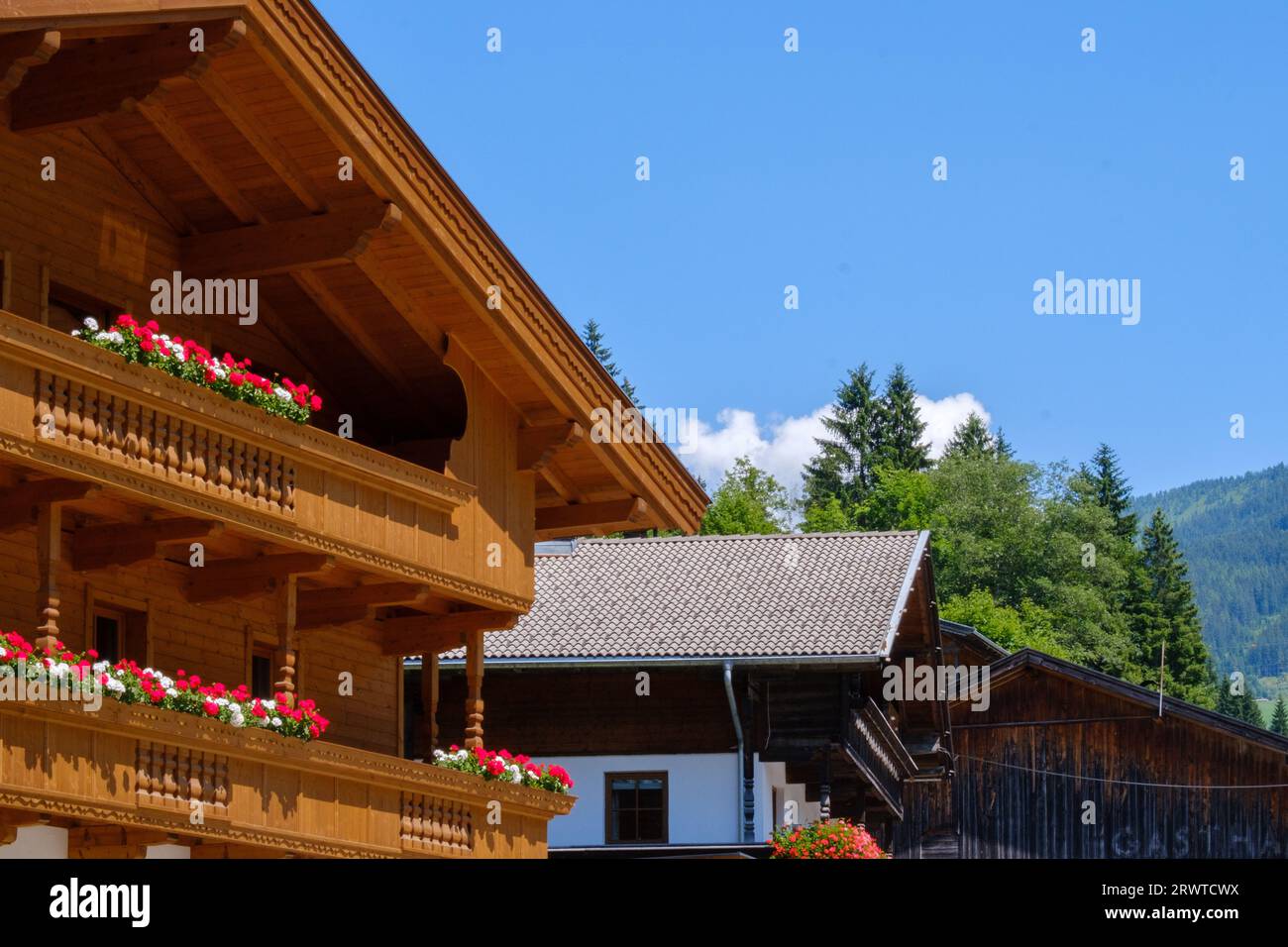 Traditional wooden Austrian house with red and white flowers on balcony ...
