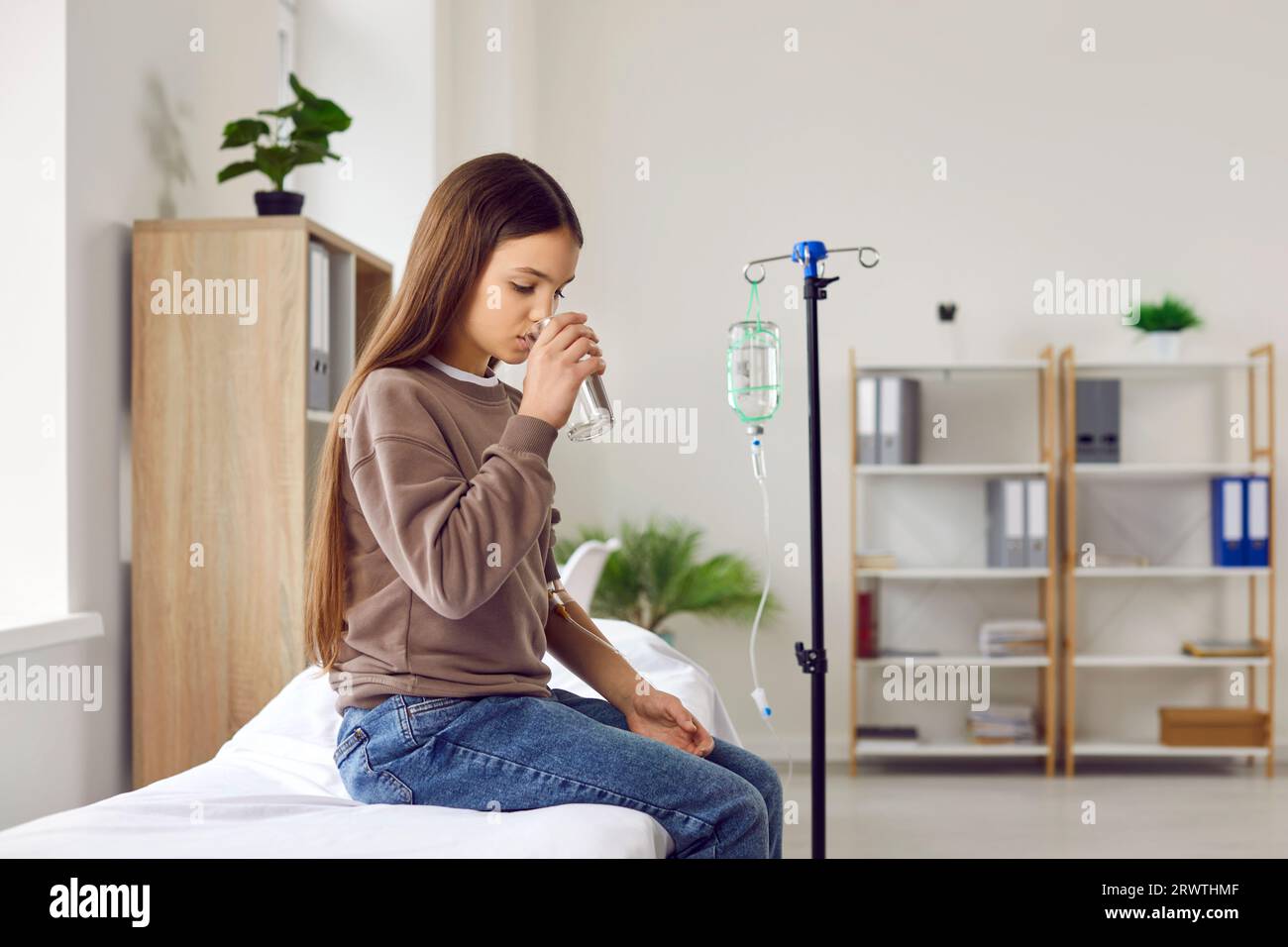 Child takes medicine with glass of water while getting medical IV line ...