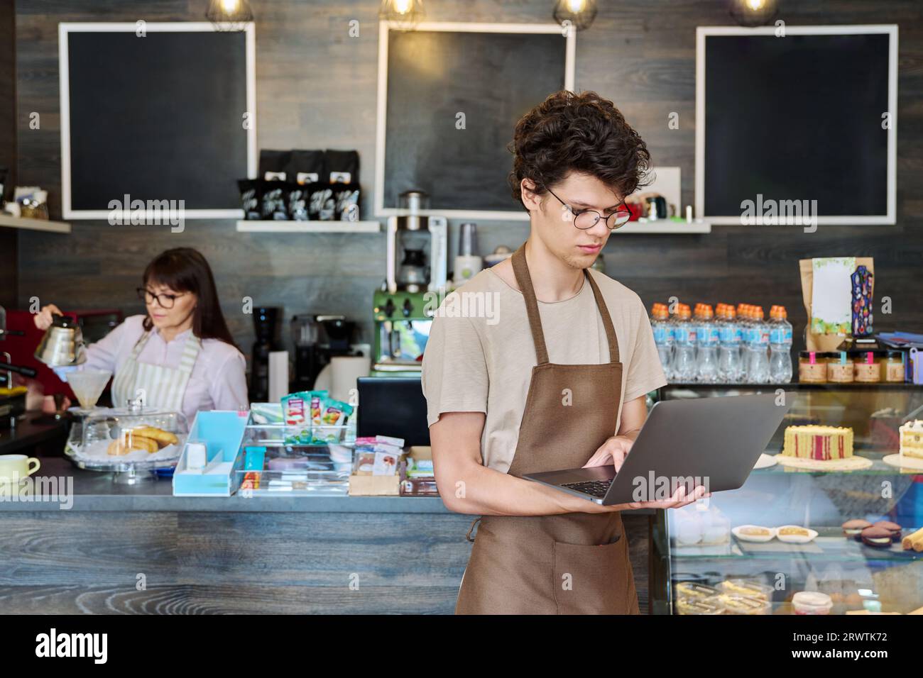 Young guy in an apron with laptop in his hands inside coffee shop ...
