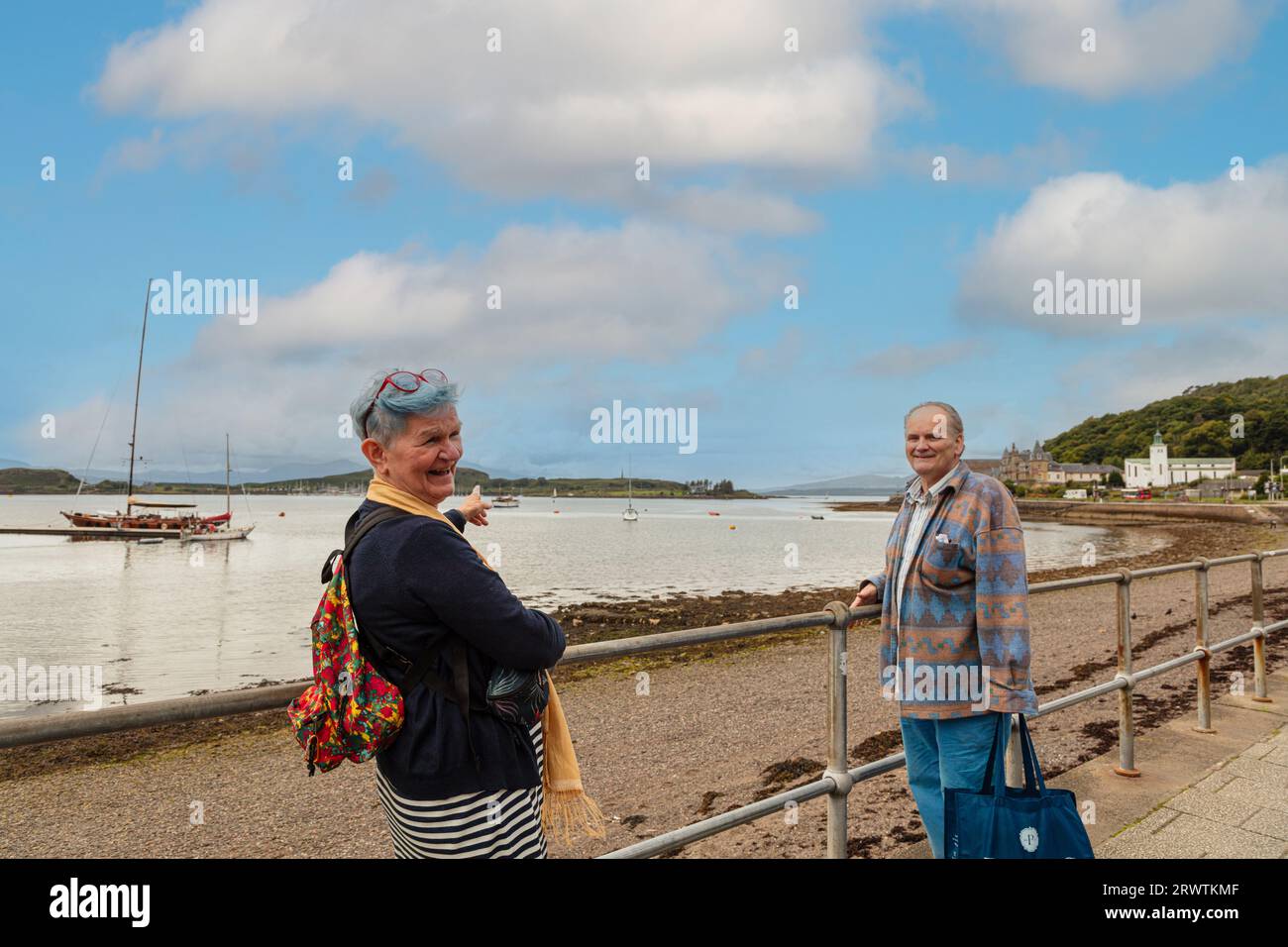 Acitve senior couple, over 60, walk along the beach sightseeing in Oban ...
