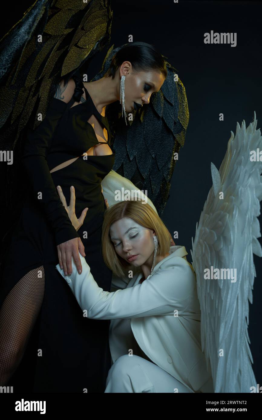 women in Halloween costumes, angel embracing dark demon on black ...
