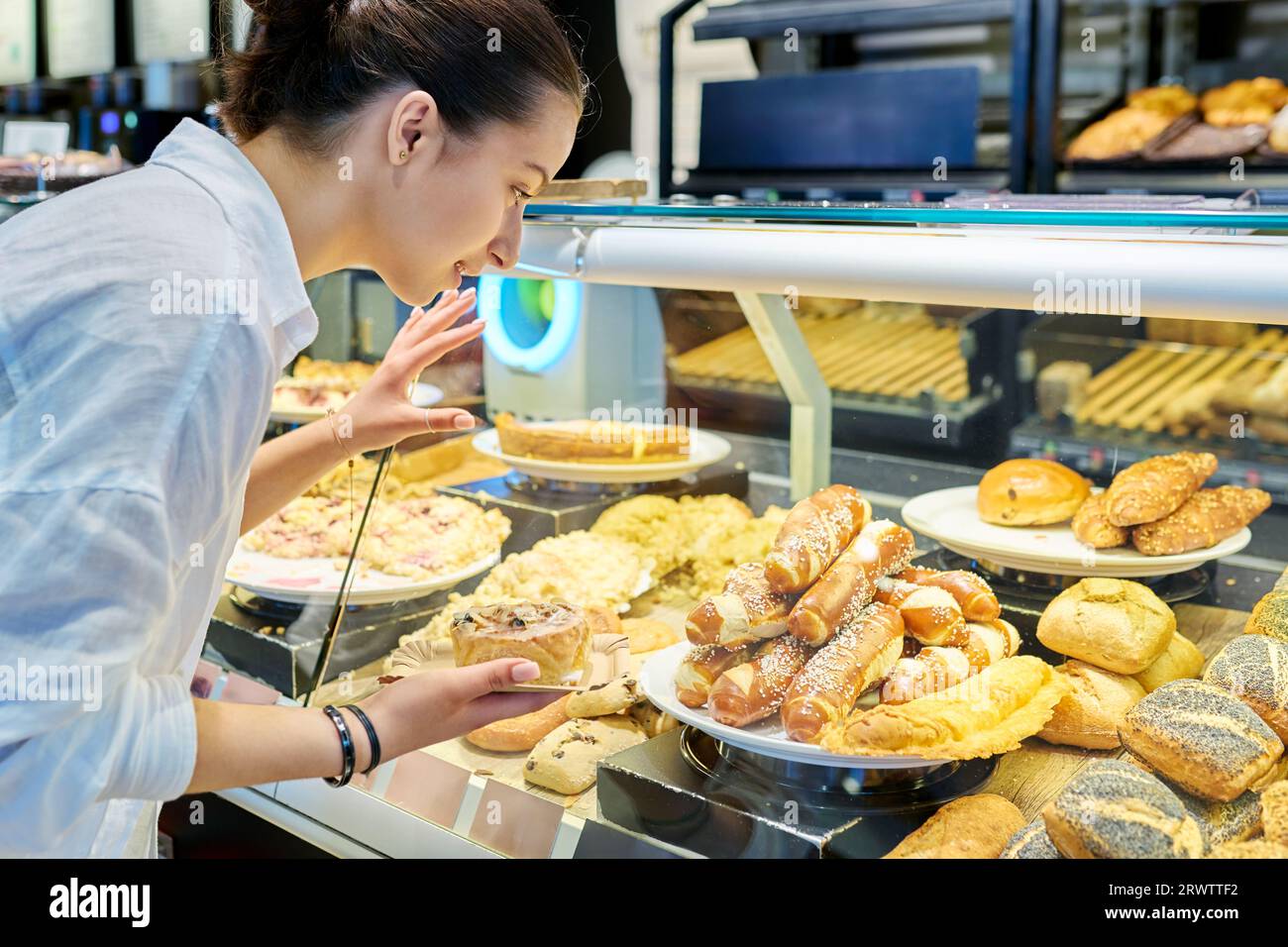 Young teenage female looking at sweet buns in glass display case in ...