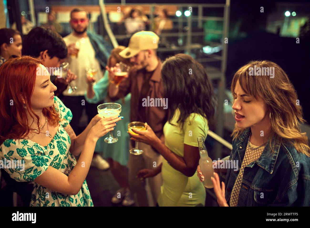 Stylish young people, friends meeting in evening outdoors, on rooftop, drinking, talking, having ...