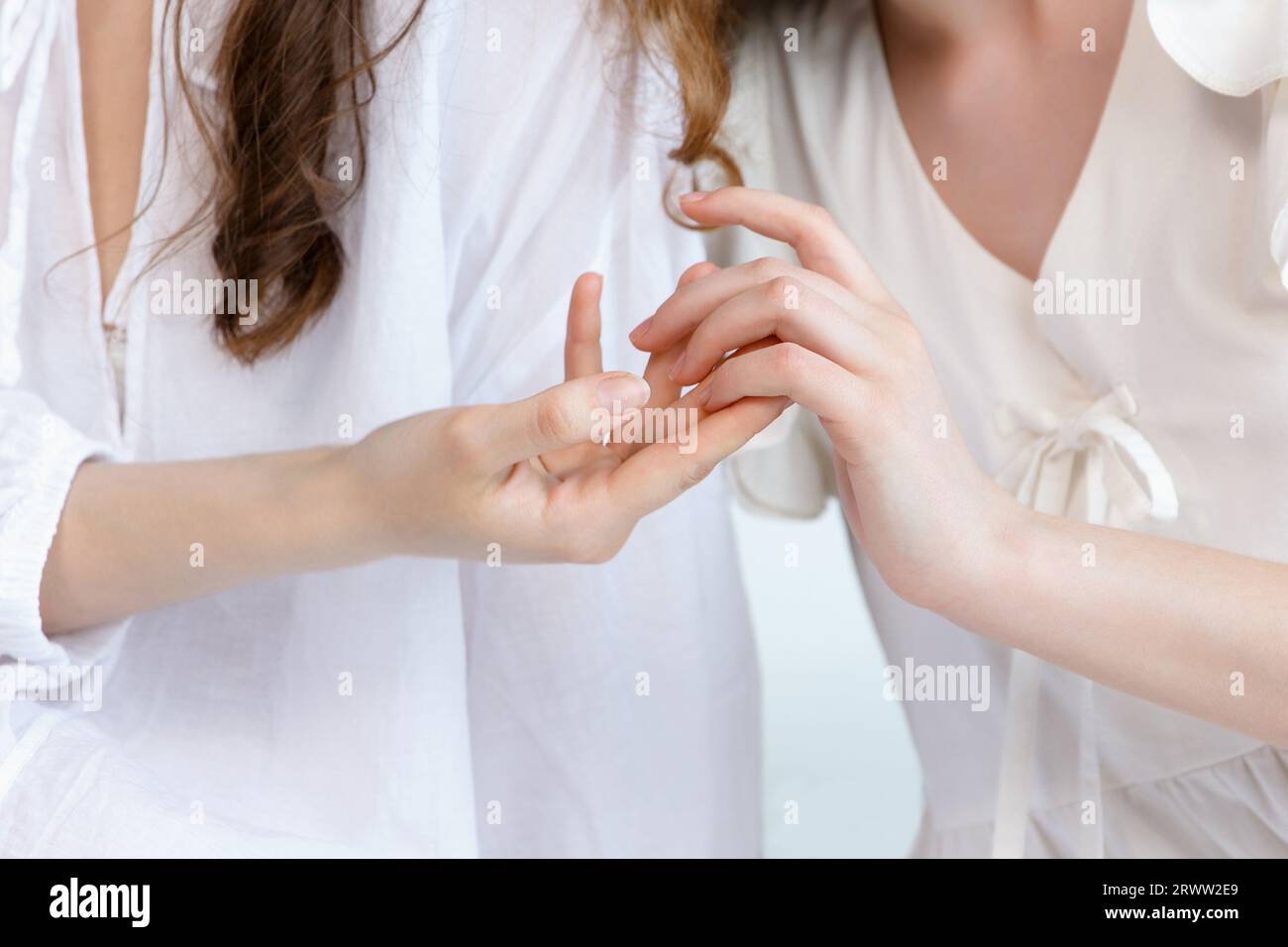 Two girls, dressed in white, touch each other's hand. Part of body ...