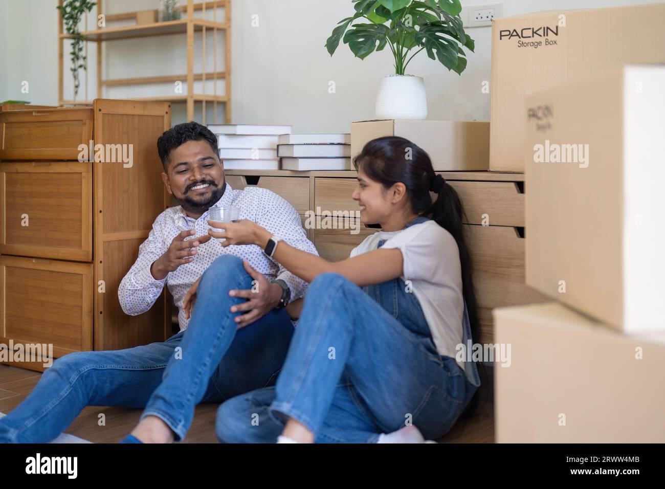 Young indian couple taking a break on moving day into new home sitting ...
