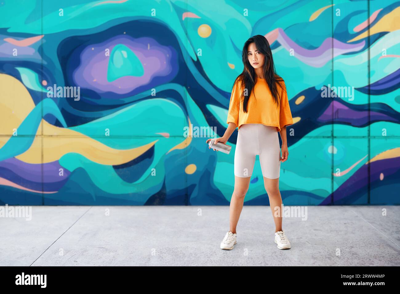 Young female graffiti painter standing near the wall with her paintings ...
