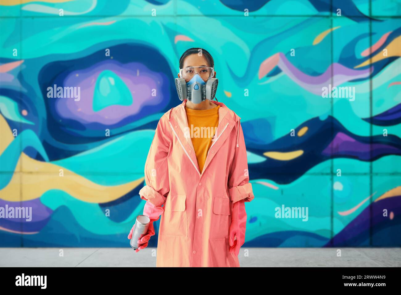 Female graffiti artist in respirator mask standing near the wall with ...