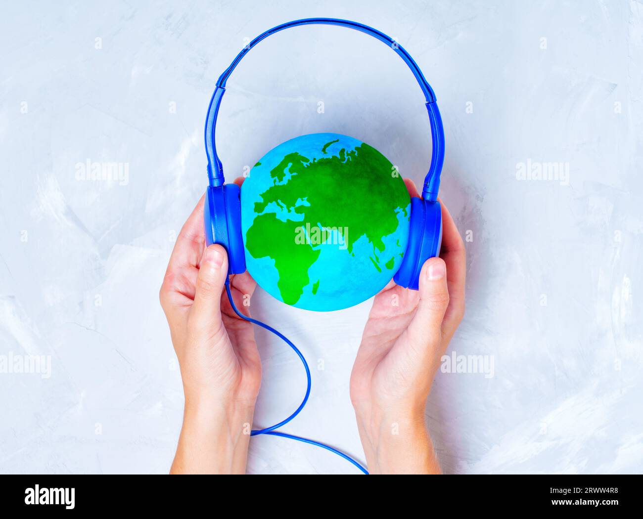 Hands placing blue headphones on a miniature globe model set against a ...