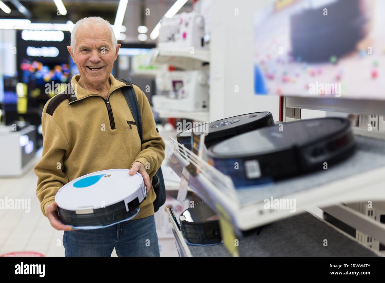 Elderly man looks at the robot vacuum cleaner behind the counter in the ...