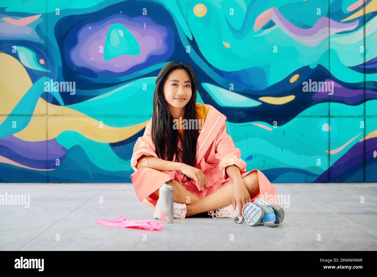 Female street artist rest sitting on the ground near the wall with her ...
