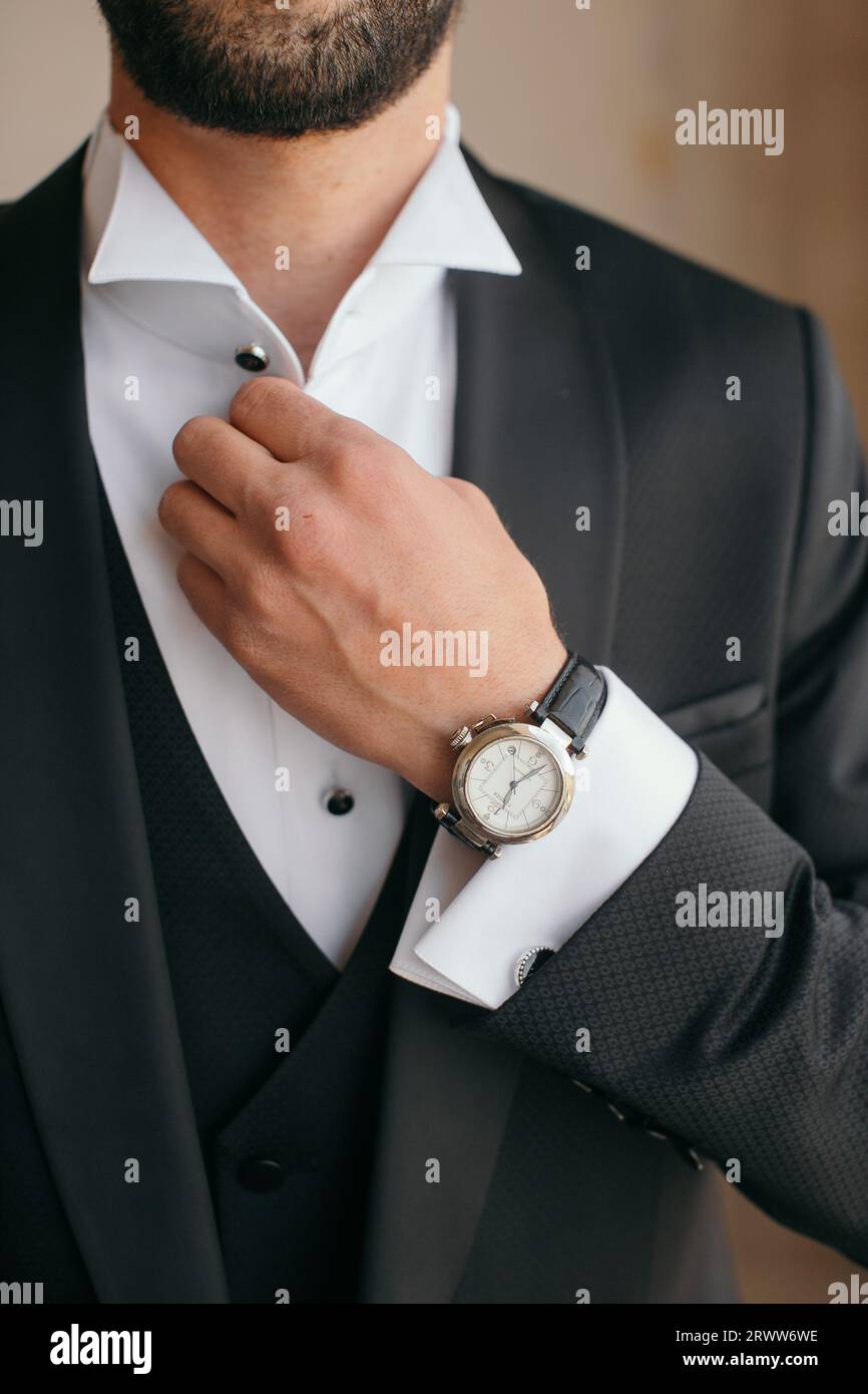 A close-up of a man's wrist with a stylish silver watch on a black suit ...