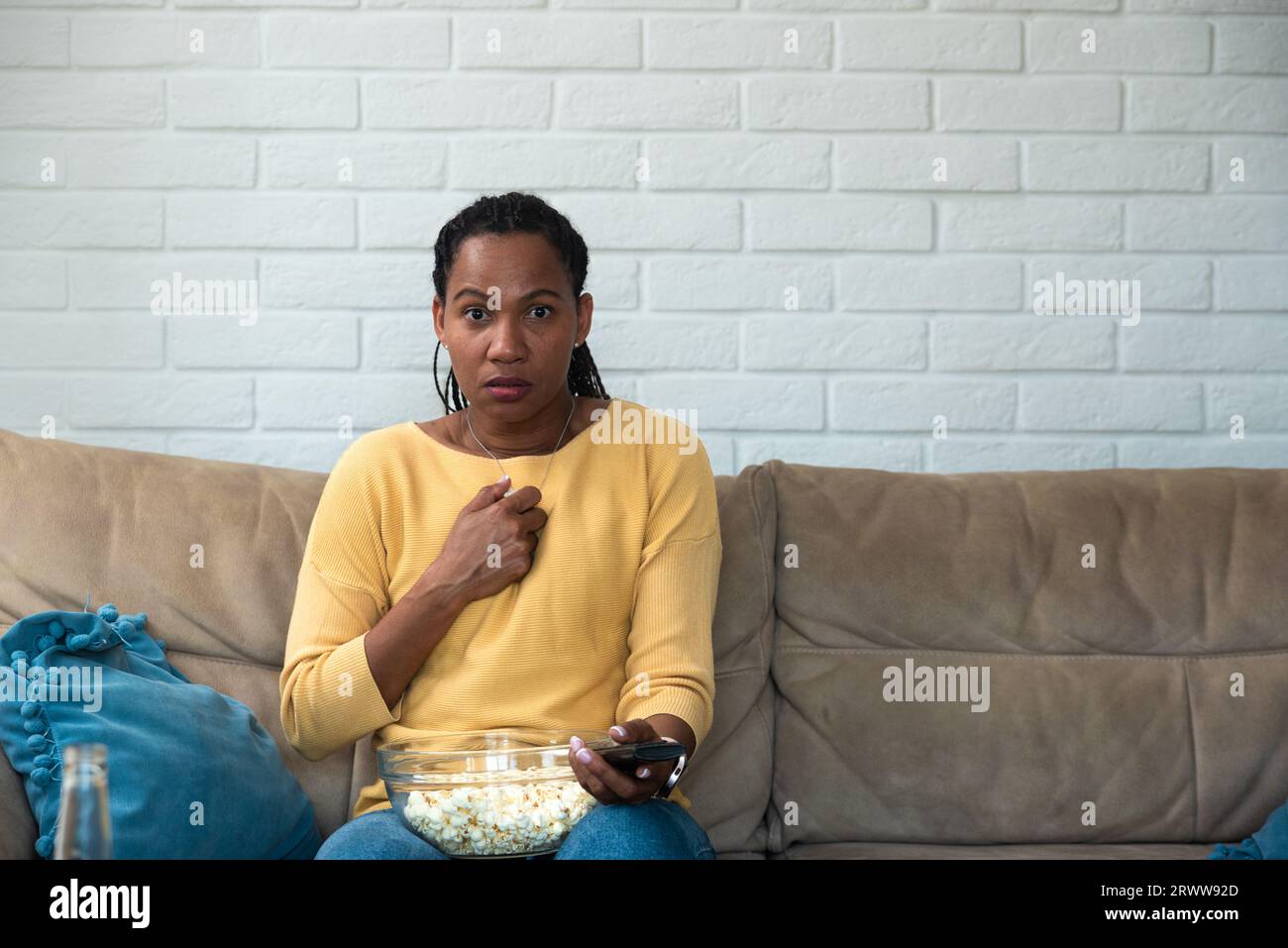 Young scared woman sitting alone at home on the sofa watching scary ...