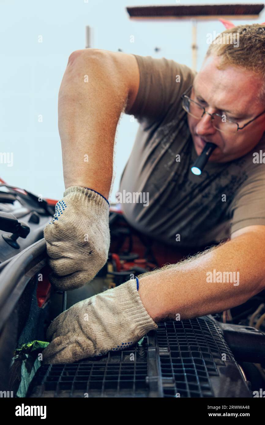 A Man with glasses Maintains a Car in a Garage. Car Repair by an ...