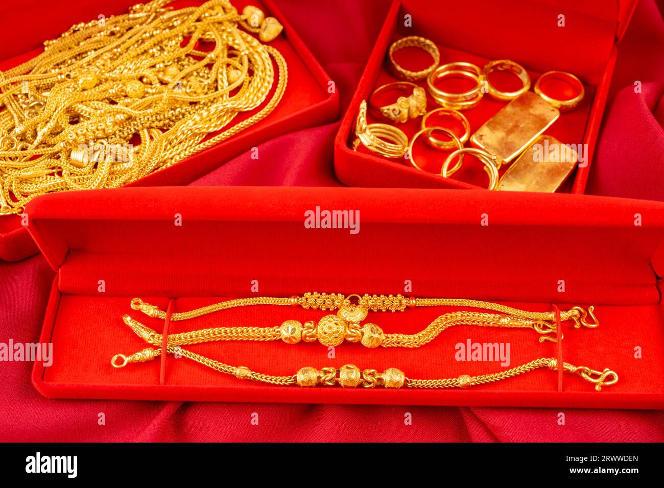 Many gold necklaces and gold bars in red box on red velvet cloth ...