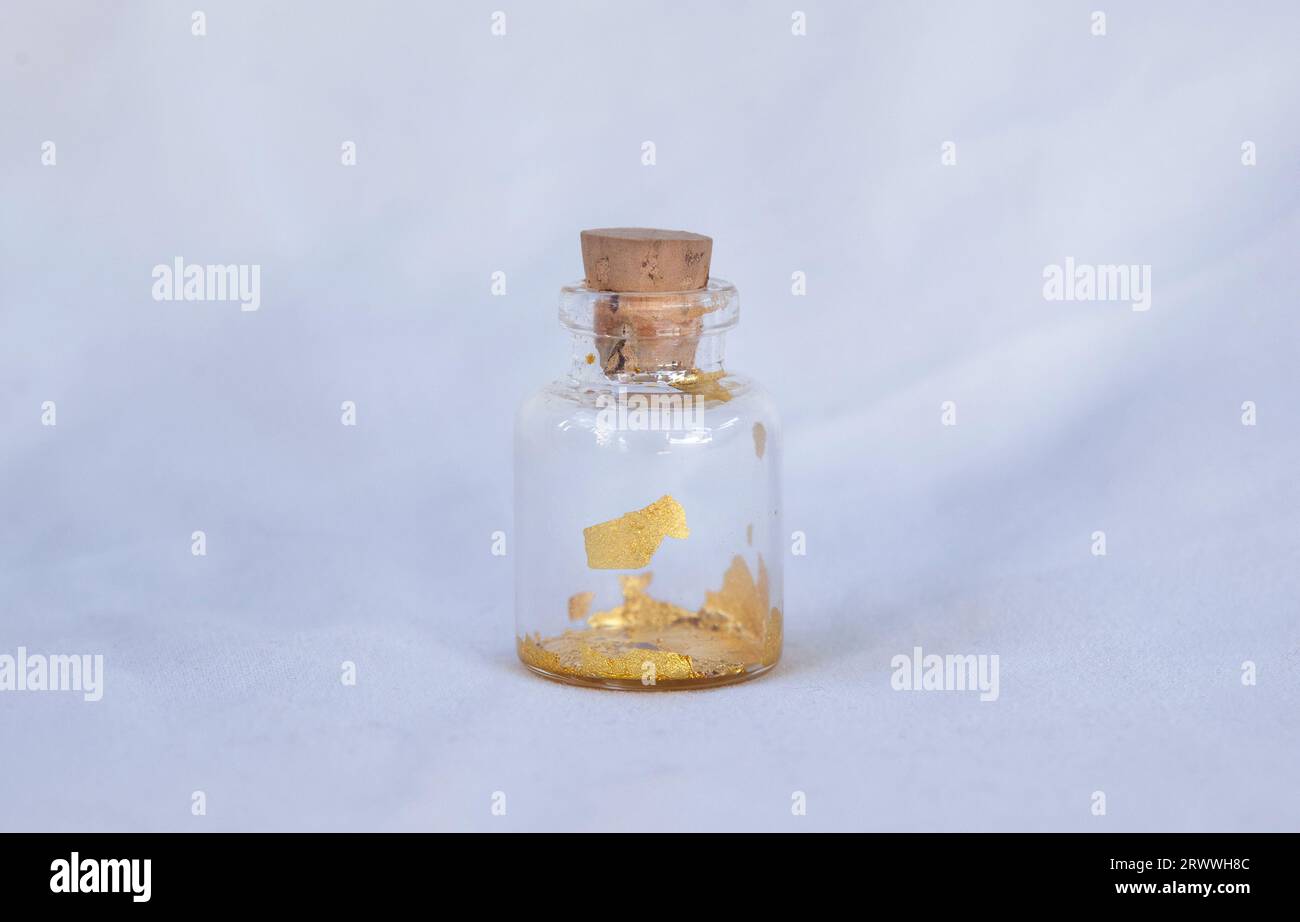 Pure gold flakes in a glass bottle. Isolated over white fabric cloth ...