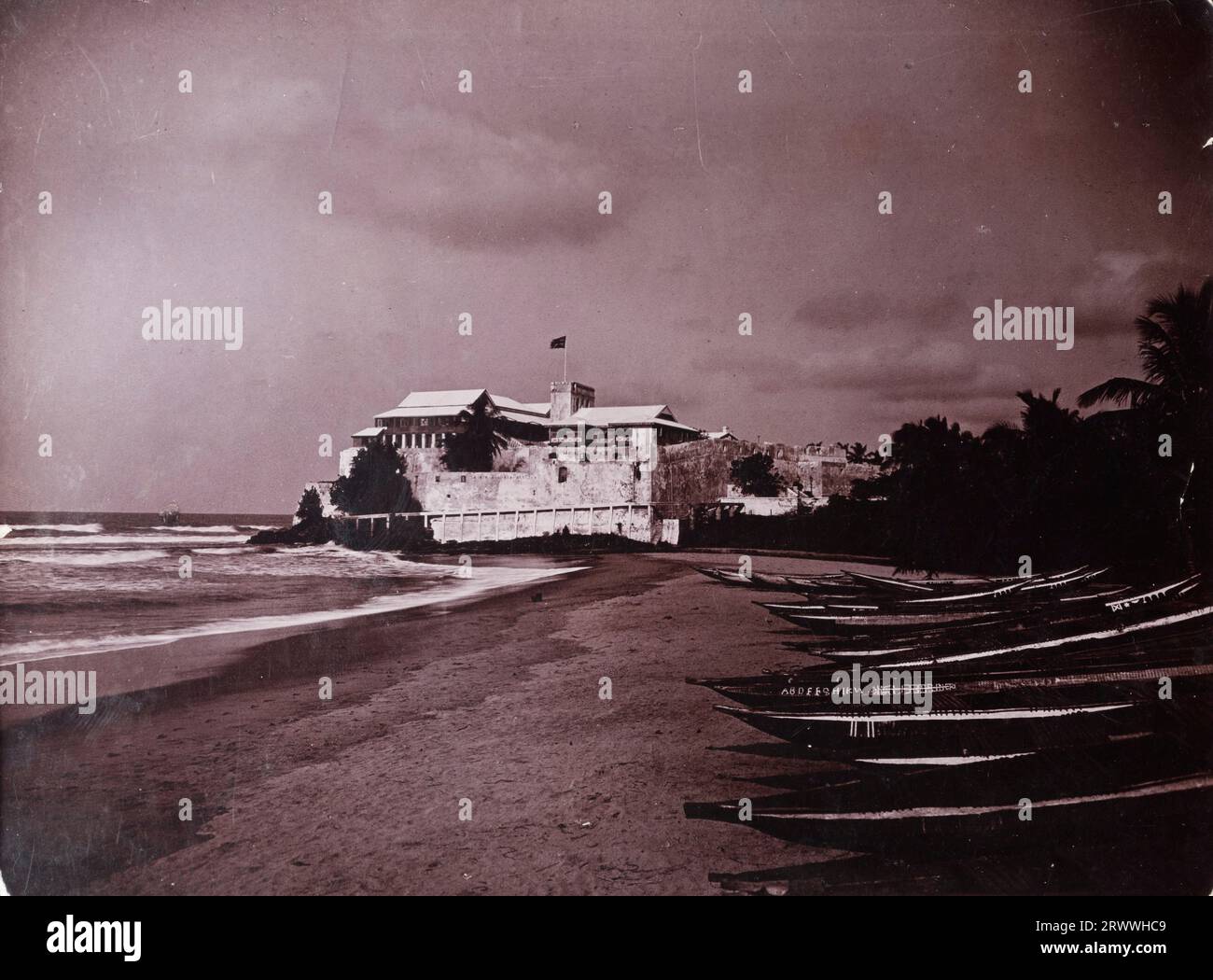 A line of canoes sit on the beach in front of Osu Castle near Accra ...