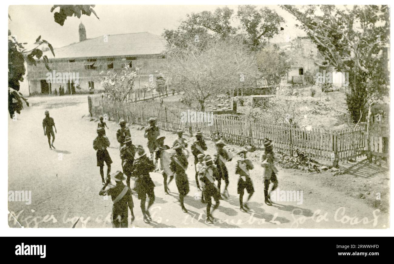A marching band of boy scouts in uniform process down a quiet road past ...