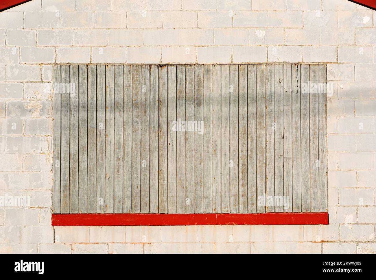 Exterior of boarded up window with a red sill in a white concrete ...