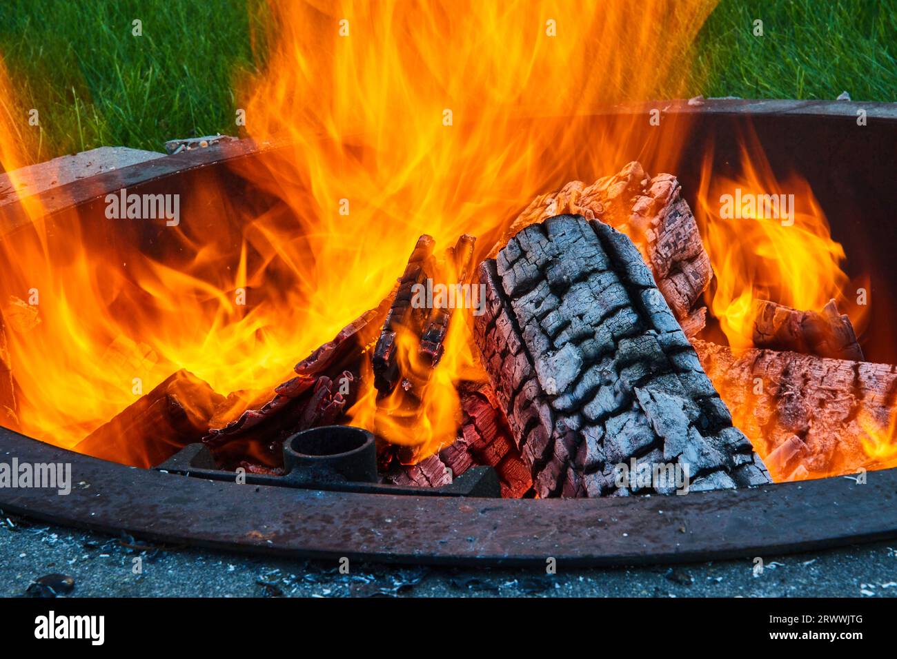 Round fire pit with intense yellow and orange flames and black log with ...