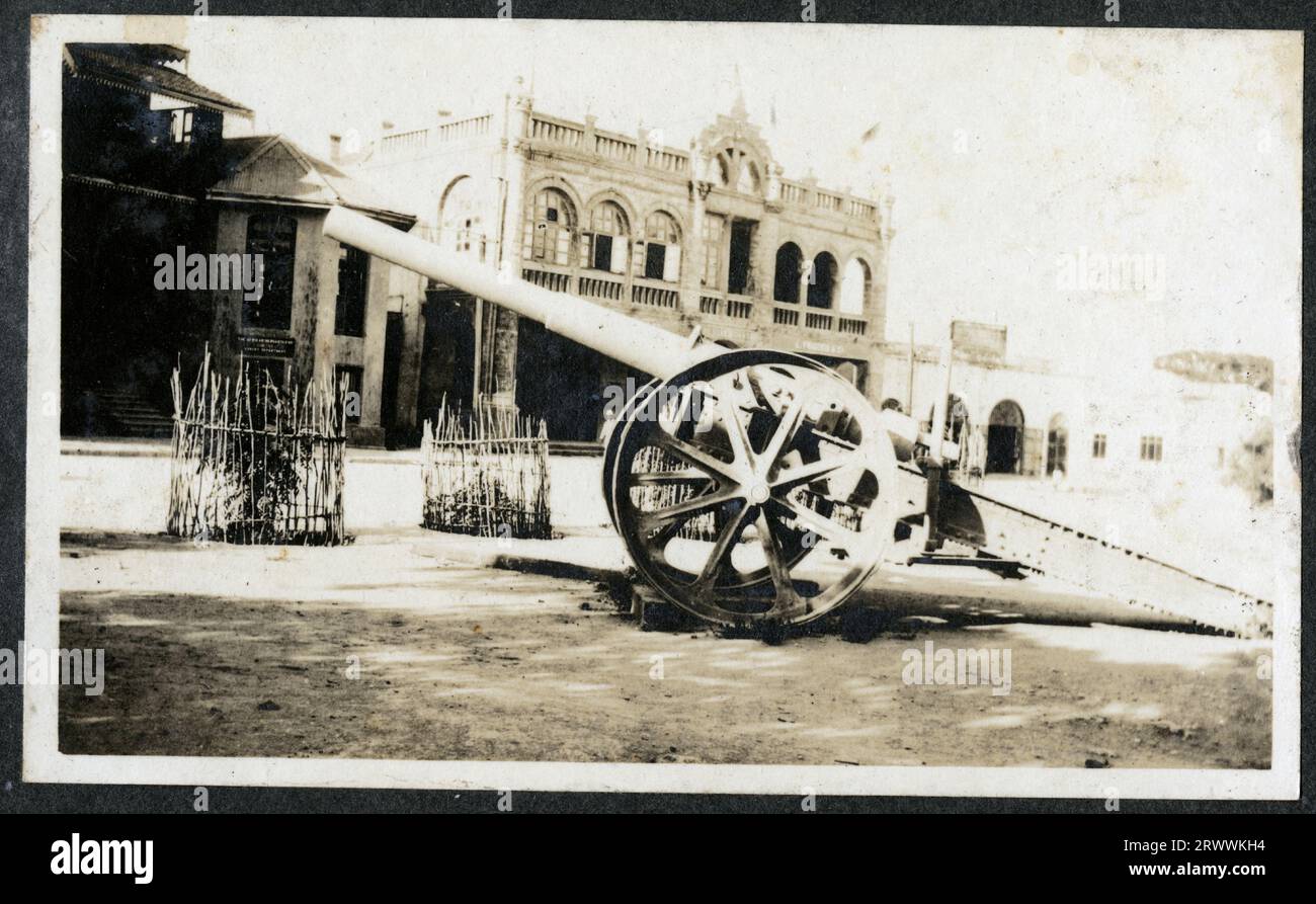 A large gun on gun carriage stands outside colonial style buildings ...