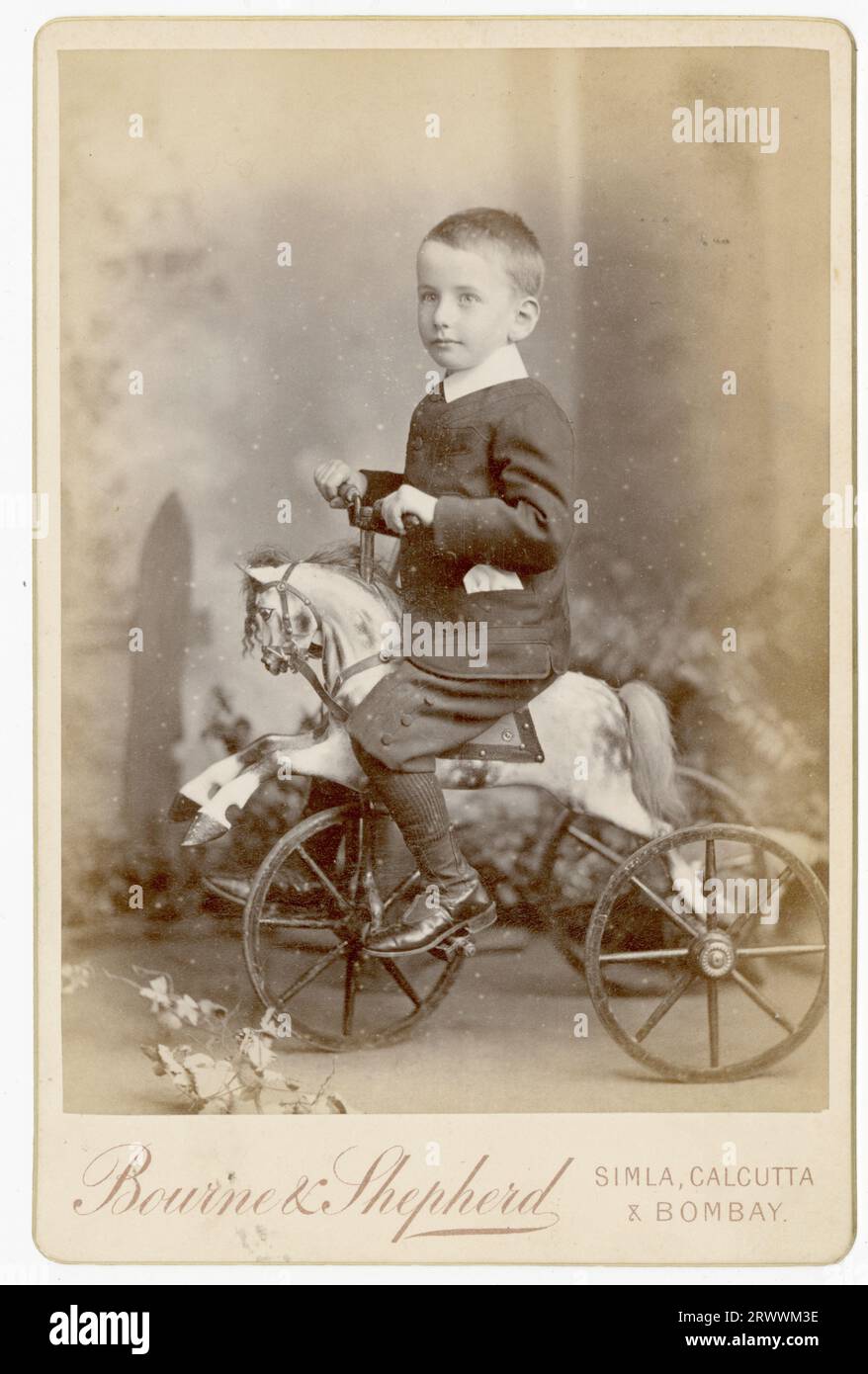 Mounted studio portrait of a young European boy riding a toy horse on ...