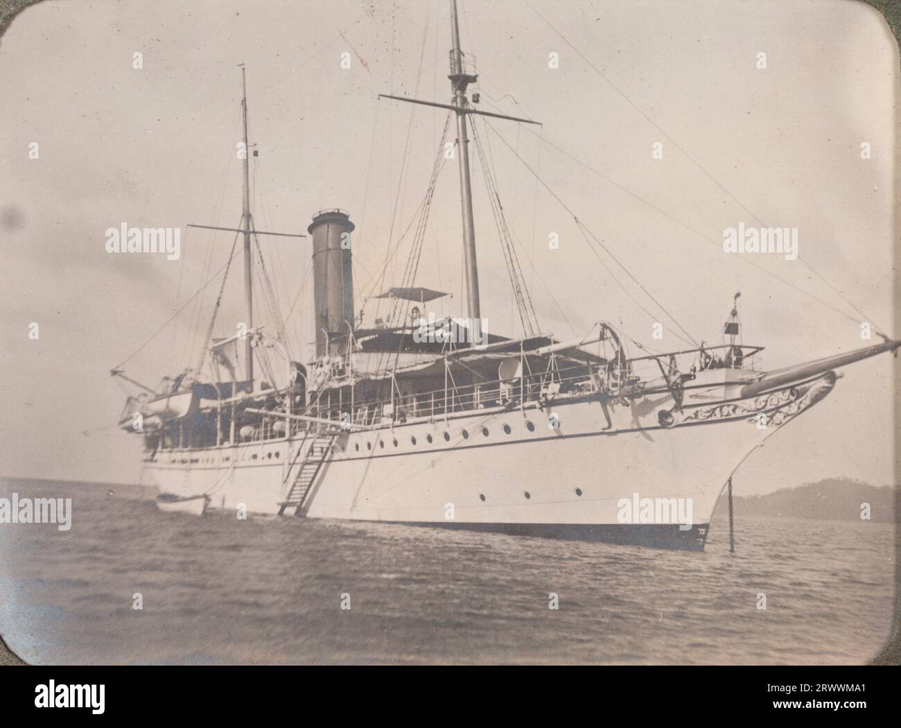 Medium sized single-funnelled, two masted ship at anchor near to land ...