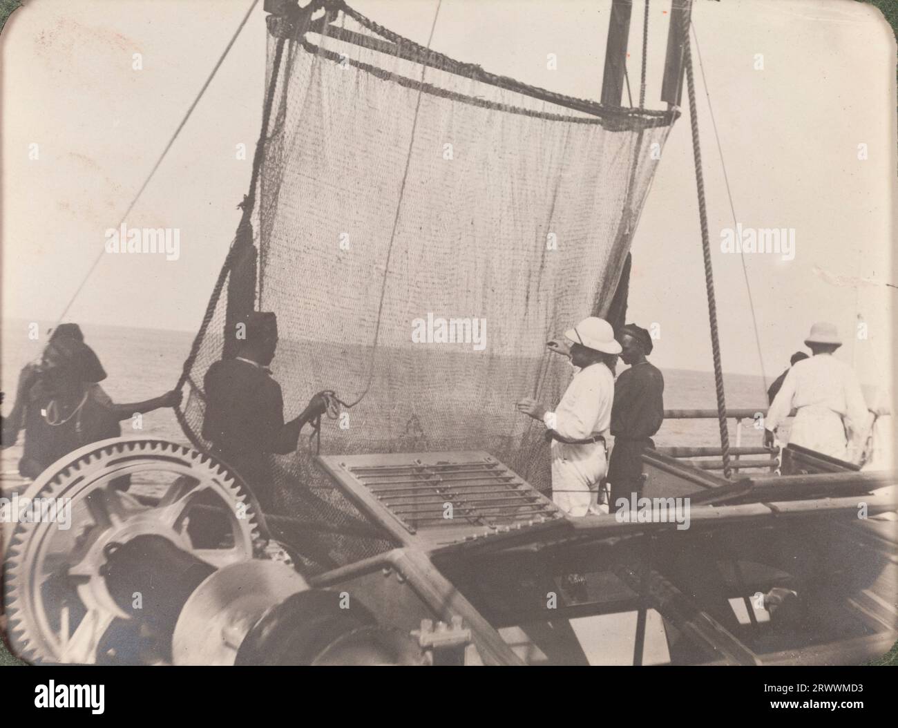 Trawl net extended by sailors and observed by officer. Caption reads ...