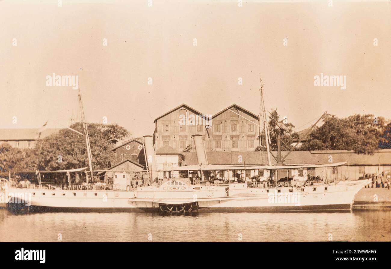 Twin-funnelled sloop moored alongside wharf at built-up waterfront ...