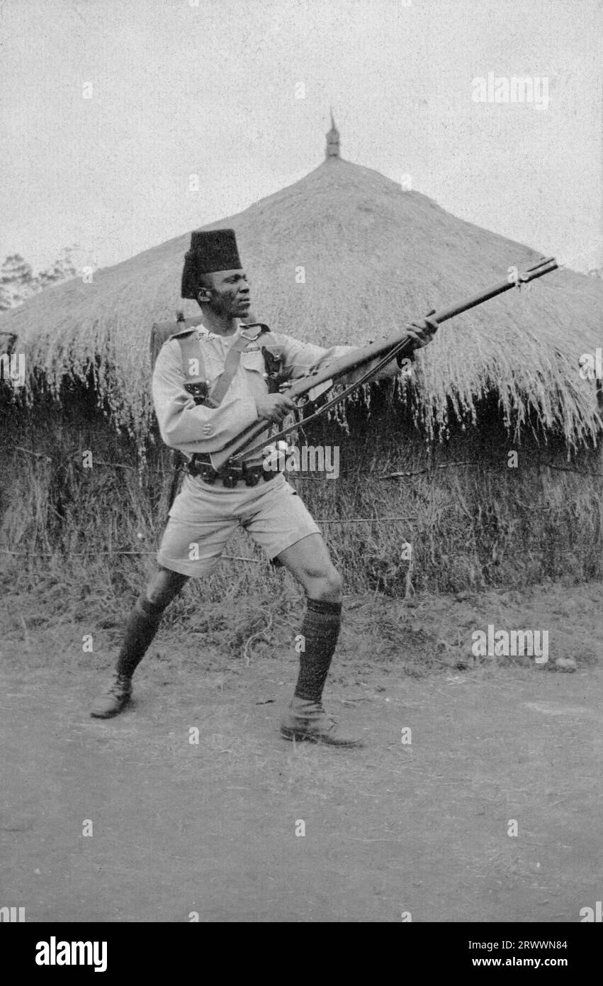 An African soldier poses in front of a thatched hut as though he is ...