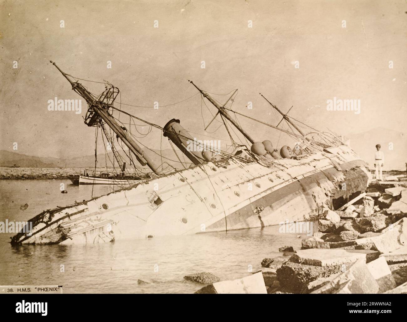 HMS Phoenix, a British naval steamship, lies upturned in shallow waters ...