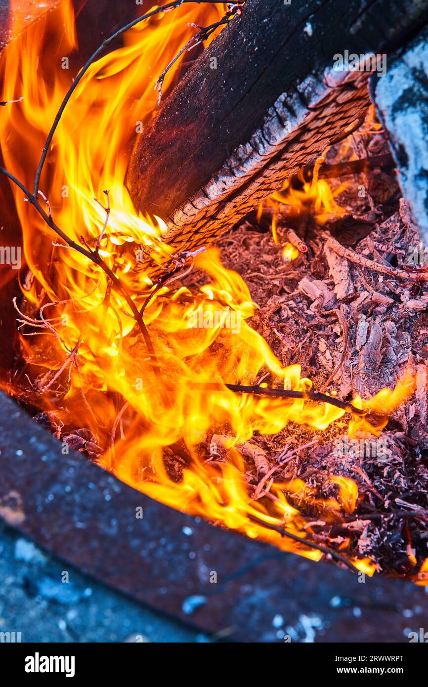 Orange and yellow flames in fire pit with white ashen log and ground ...