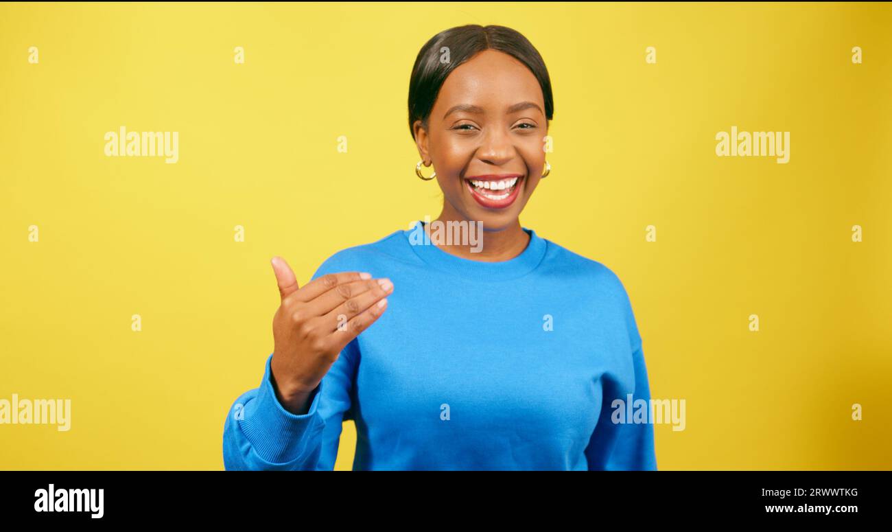 Friendly young woman beckons with hand 'come here', yellow studio ...